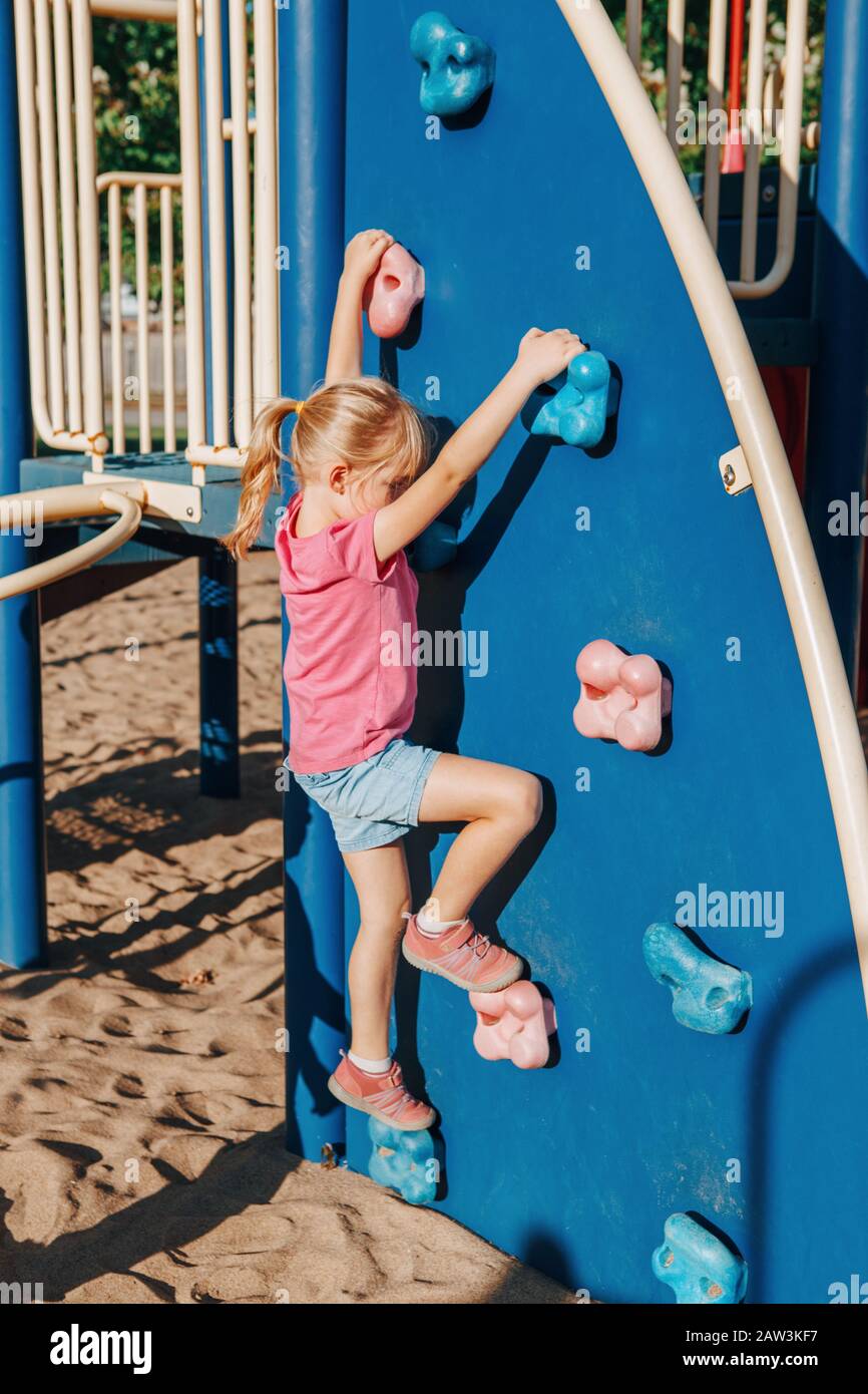 Little preschool girl climbing rock wall at playground outside on ...