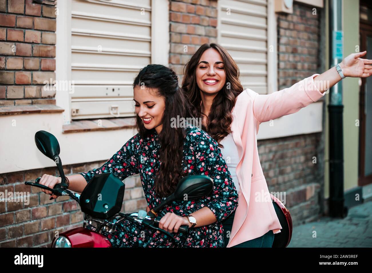 Having great fun together. Two happy female friends riding on motorbike ...