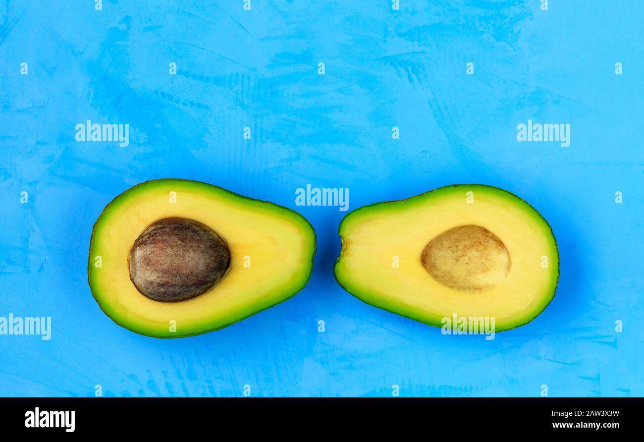 Avocado cut in half, one slice with core on a light turquoise surface ...