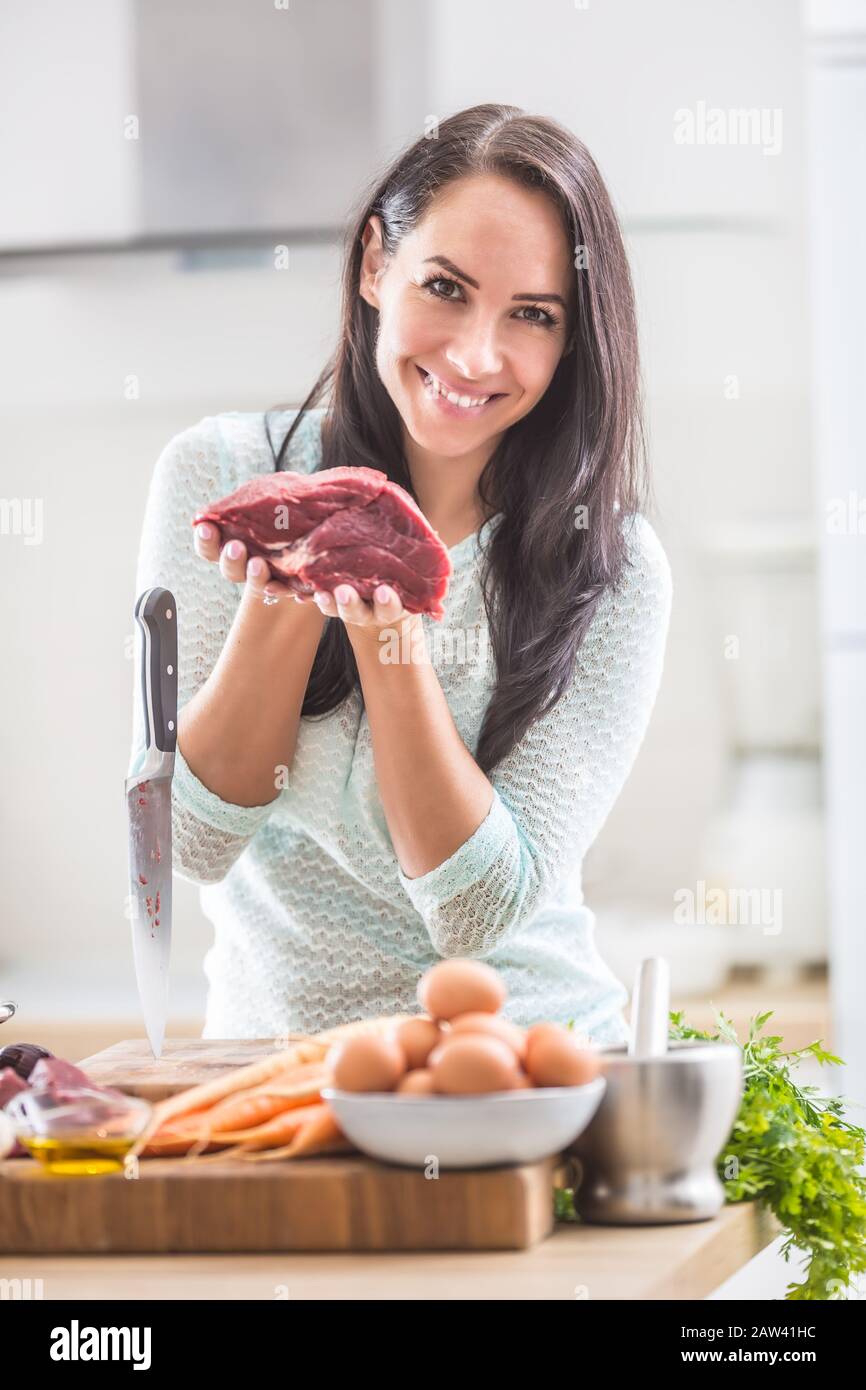 Cheerful female cook in kitchen holding raw beef meat Stock Photo - Alamy