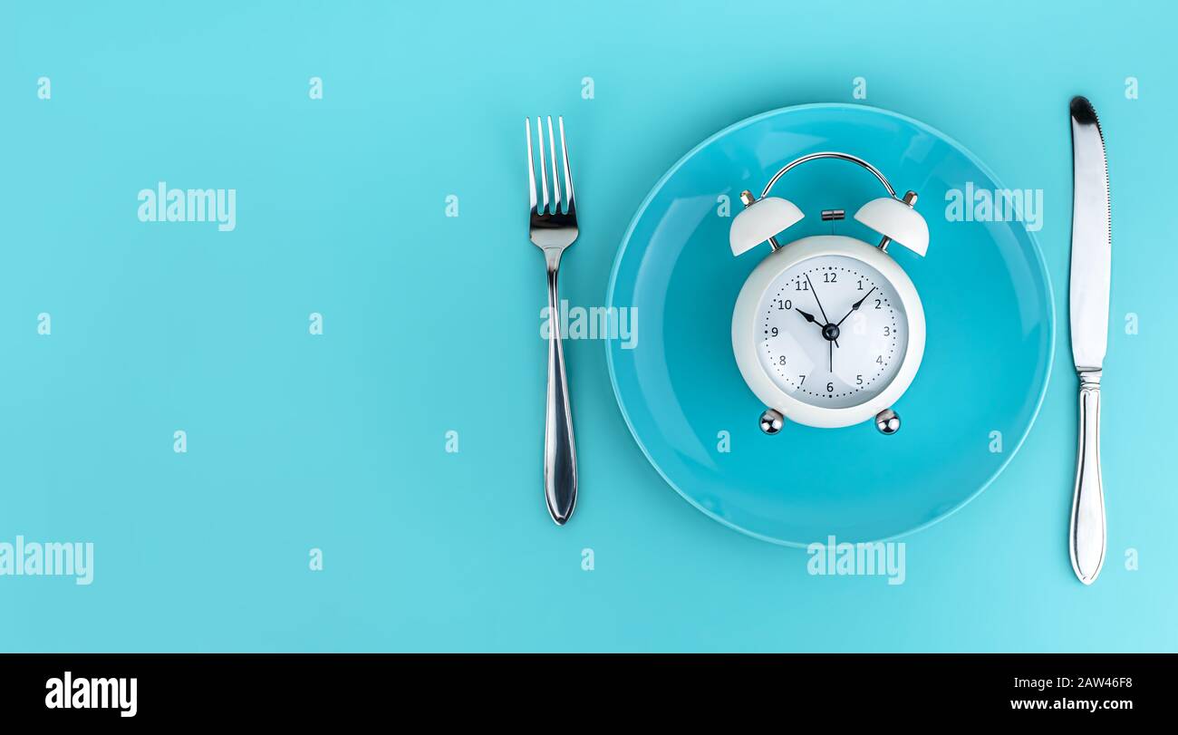 Alarm clock with fork and knife on the light blue background. Time to ...