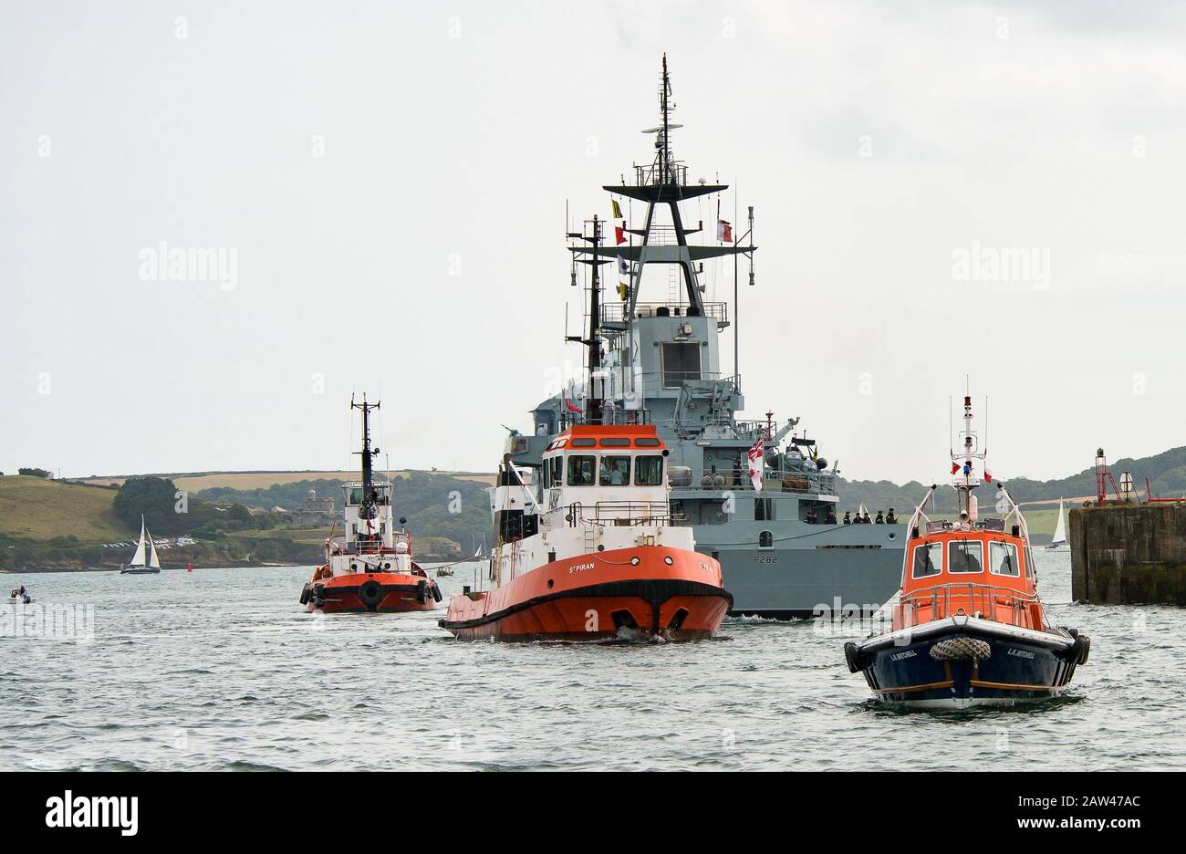 Massive grey battleship being towed into Falmouth docks by bright ...