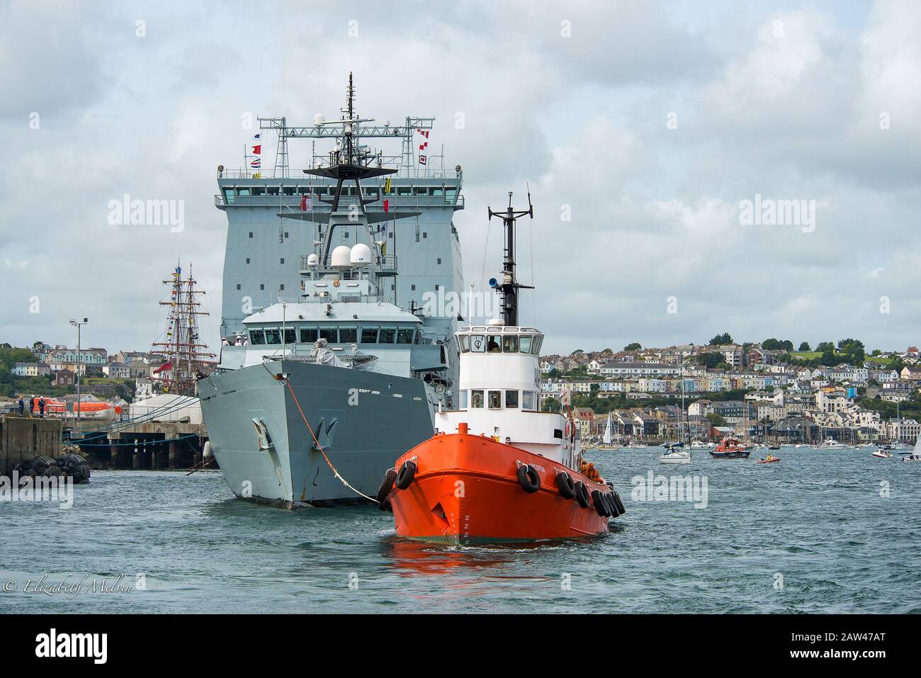 Bright orange pilot boat tug guiding the huge grey battleships to their ...