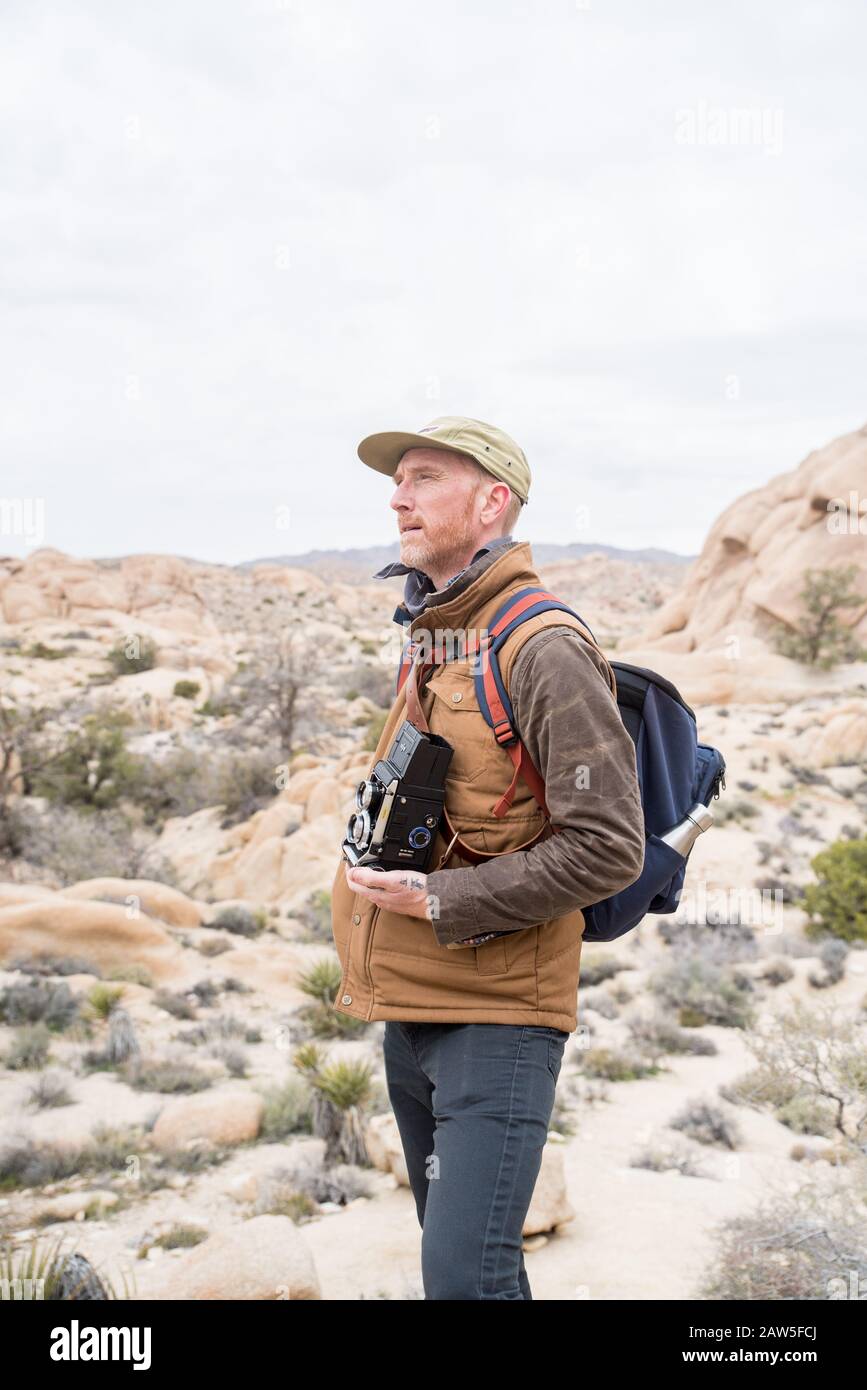 Man with billed hat and camera in desert by stones and plant life Stock ...