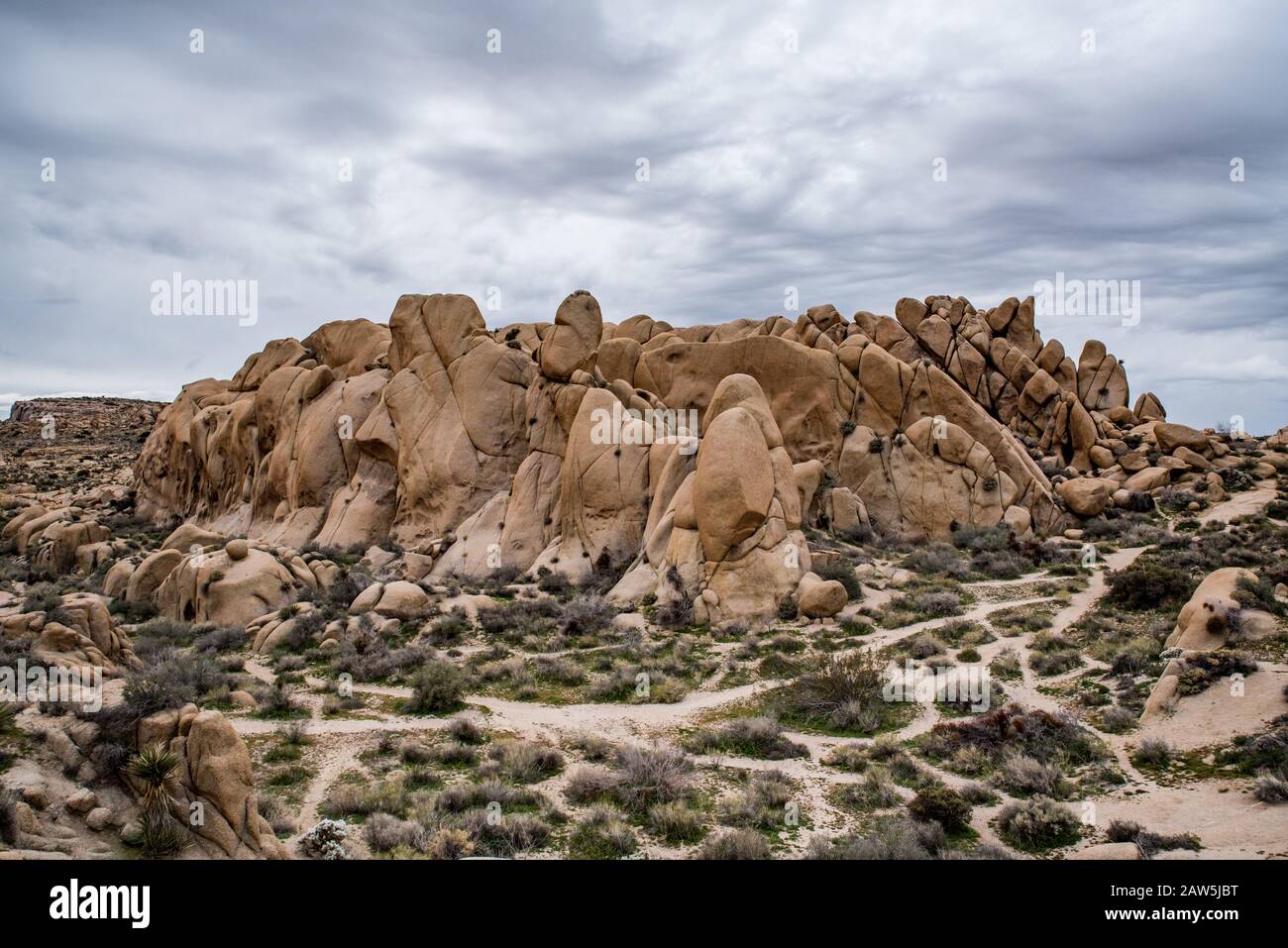 Massive boulder mound in center of desert landscape under cloudy sky ...