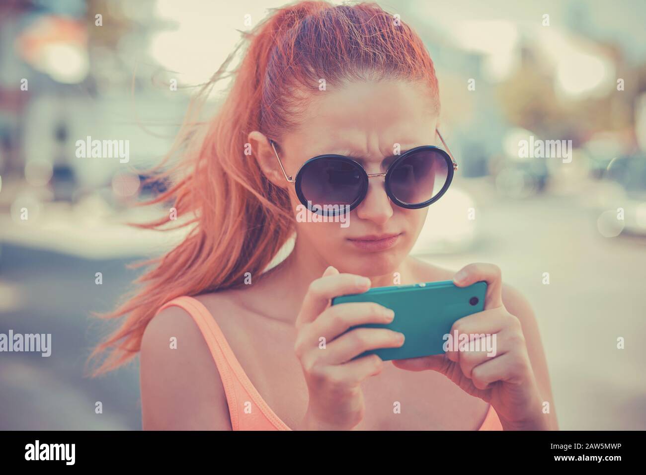Portrait of an annoyed and frustrated young woman looking at phone ...