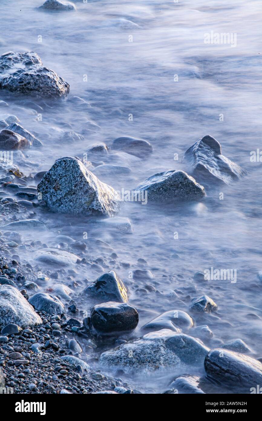 Misty waves on a rocky beach at dawn Stock Photo - Alamy
