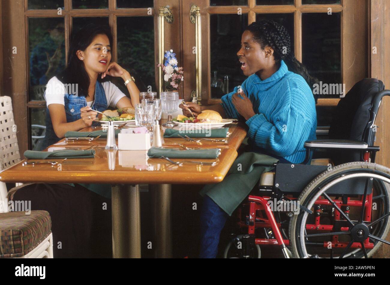 Handicapped woman in wheelchair and friend having dinner in restaurant ...