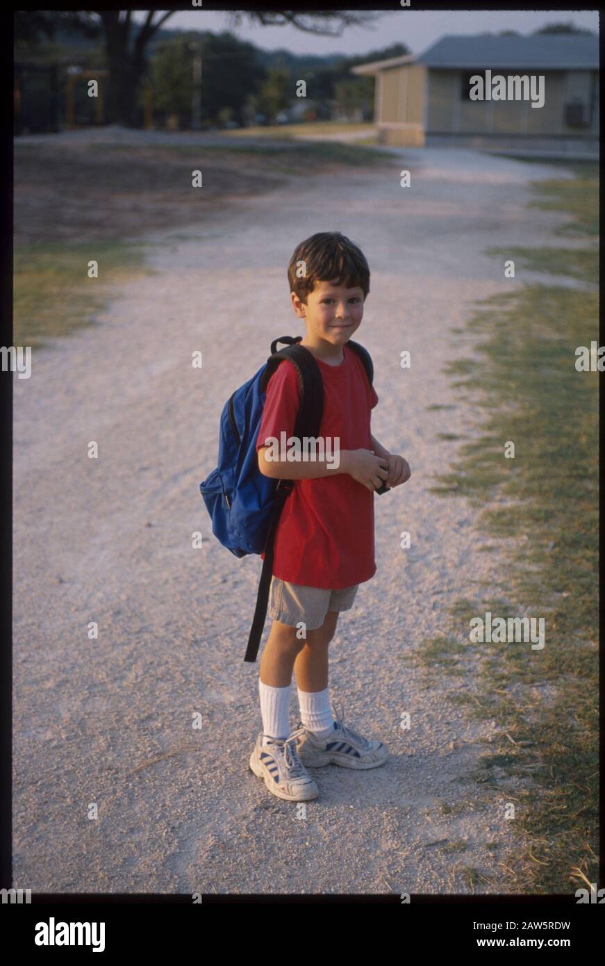 Anglo boy in kindergarten wears backpack while walking on path to ...