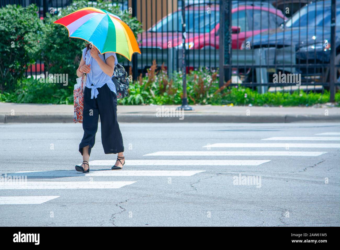 A young lady uses a colorful rainbow umbrella to shield herself from ...