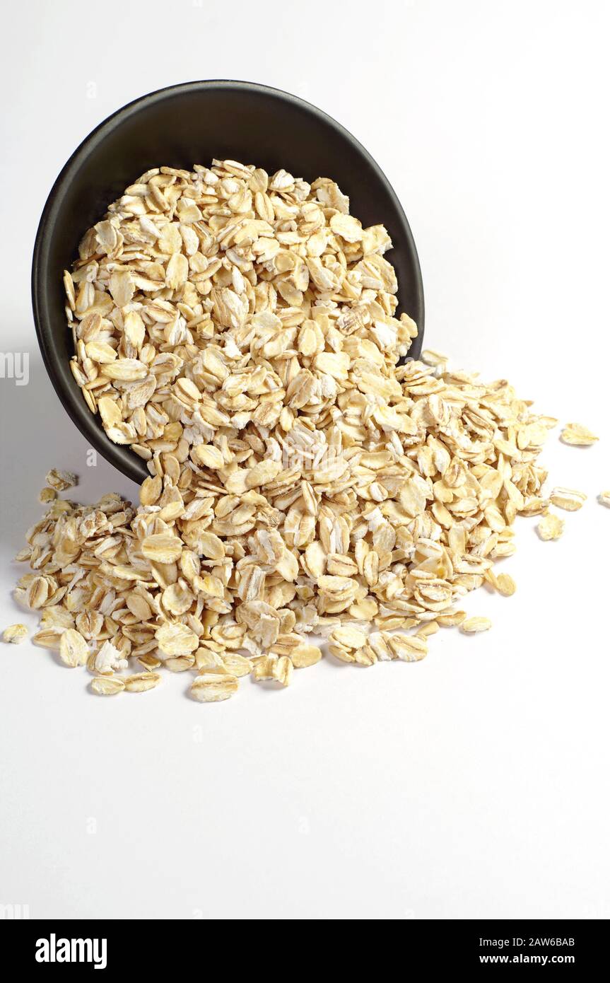 Oatmeal spilling from black bowl on a white background Stock Photo - Alamy