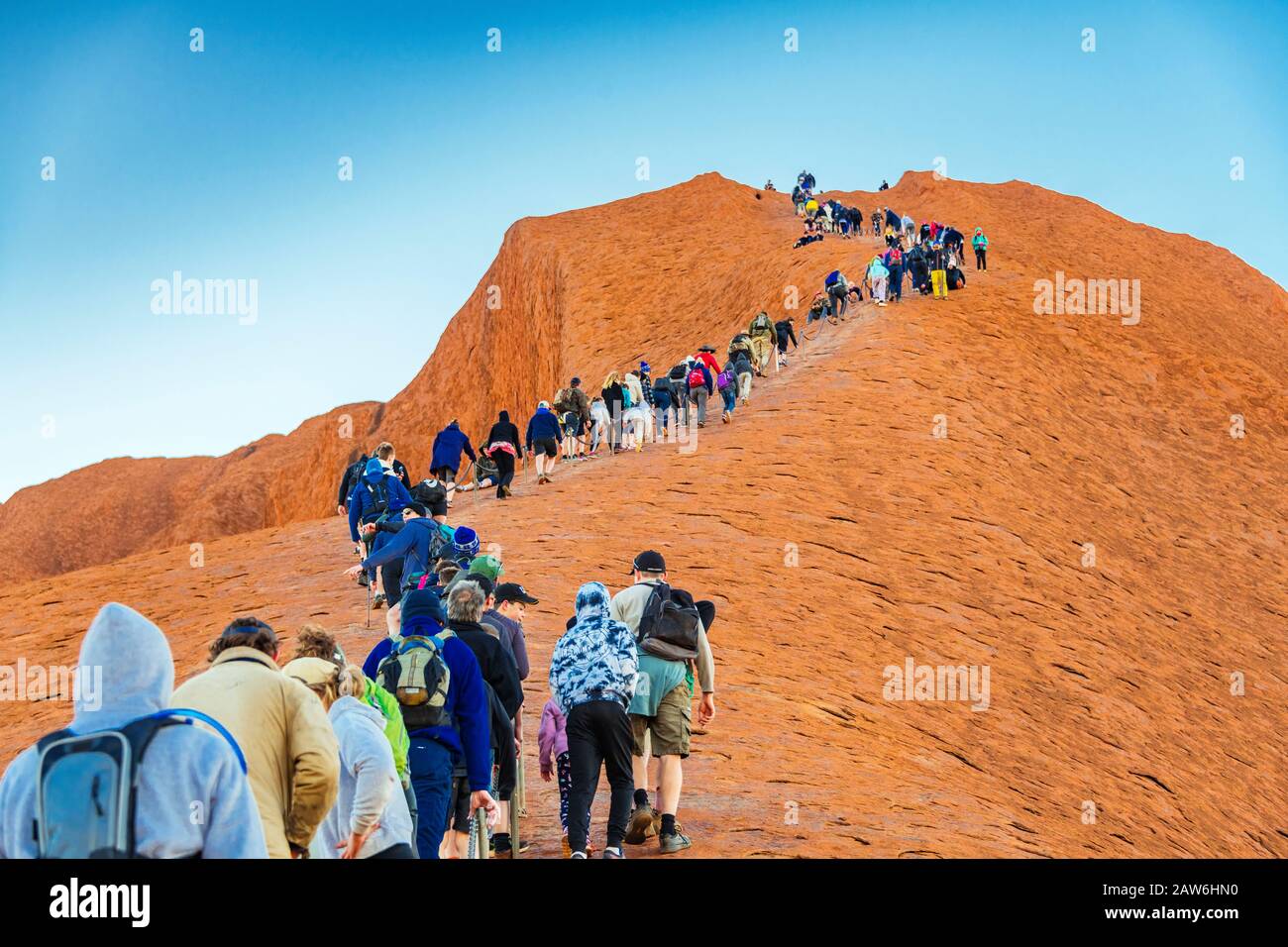 Tourists climb the steep side of Uluru whilst grasping the chain ...