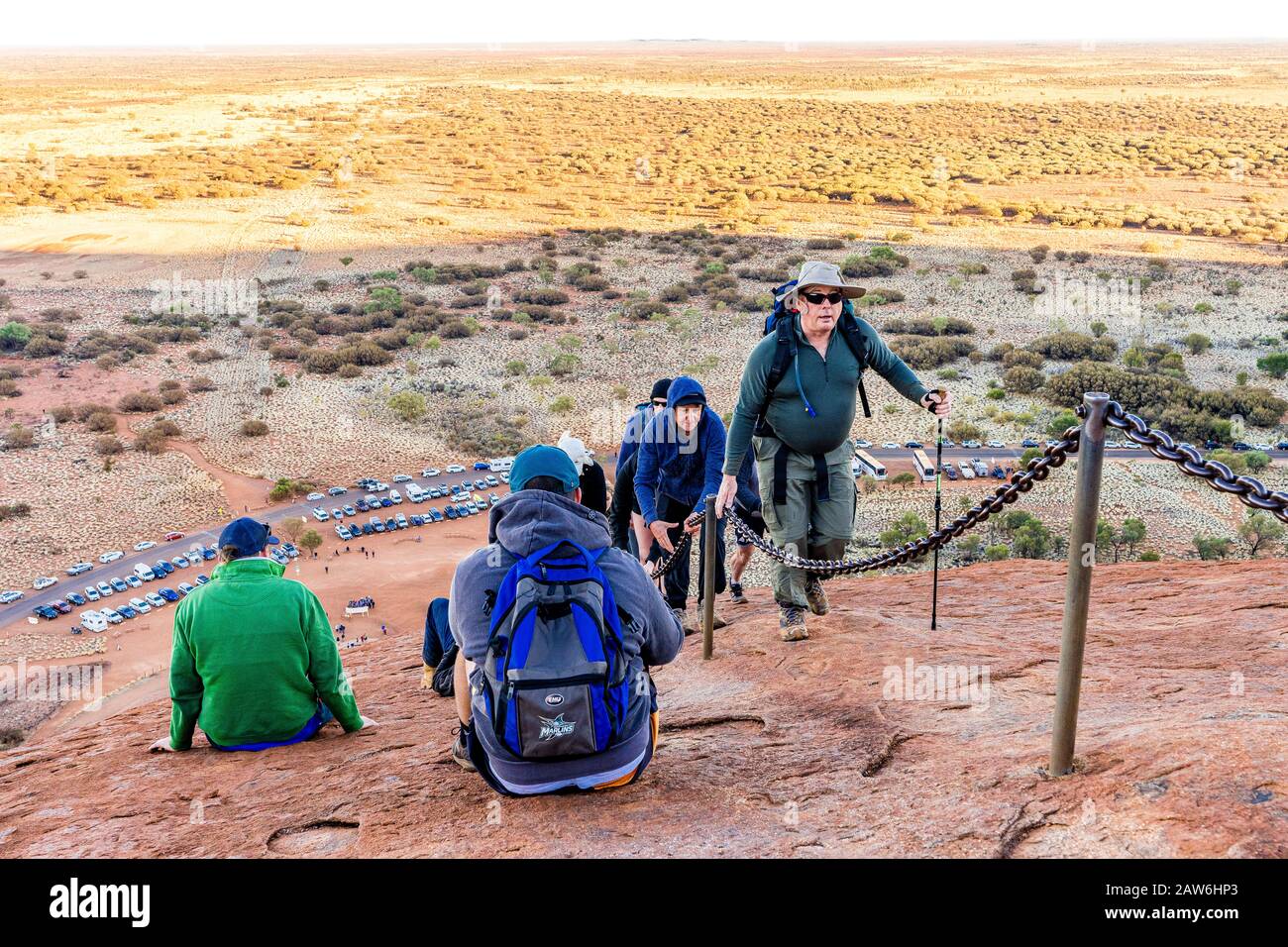 Tourists climb the steep side of Uluru whilst grasping the chain ...