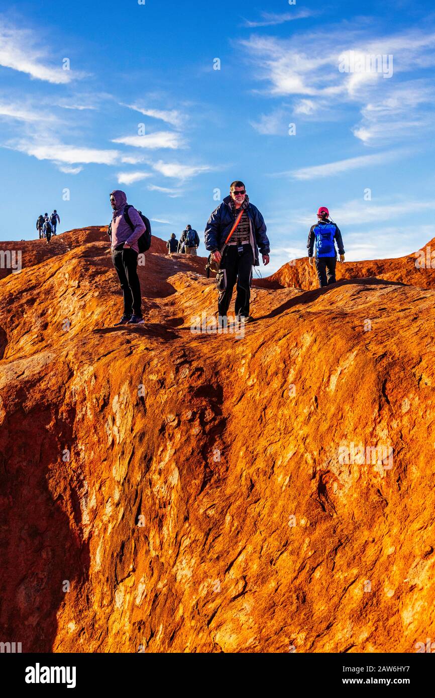 Tourists climb over the steep undulating terrain on top of Uluru ...