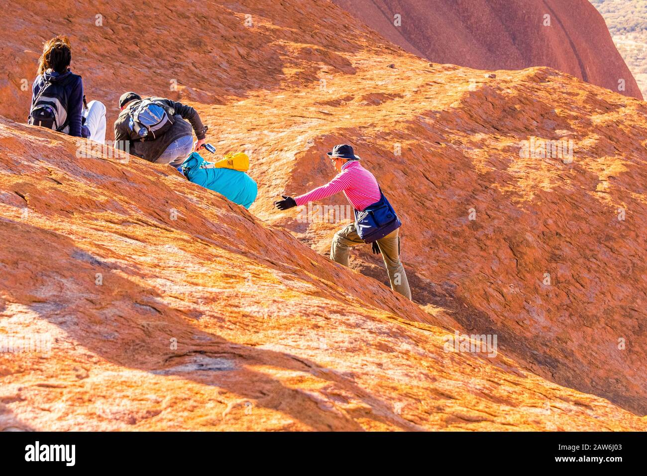 Tourists climb over the steep undulating terrain on top of Uluru ...