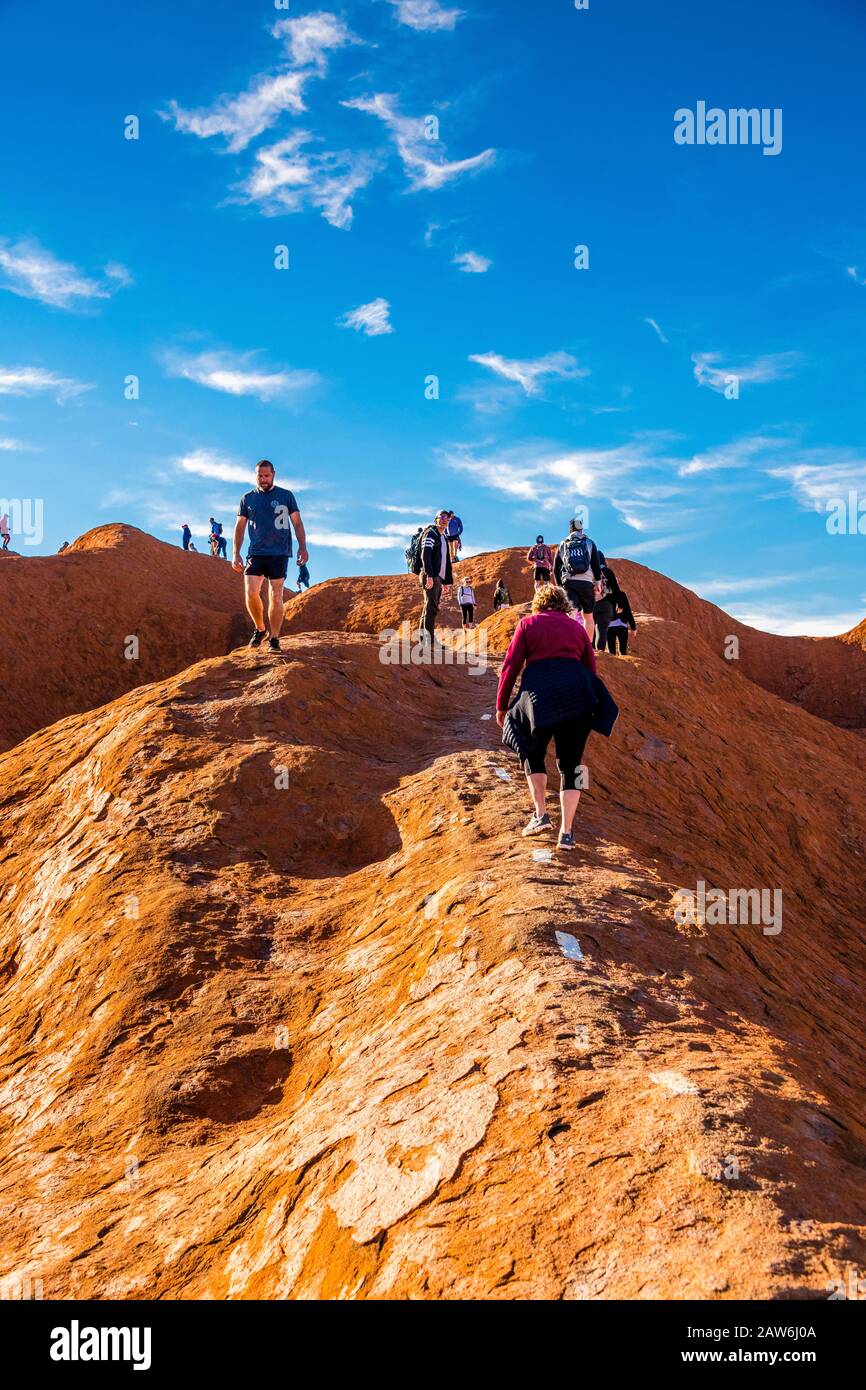 Tourists climb over the steep undulating terrain on top of Uluru ...