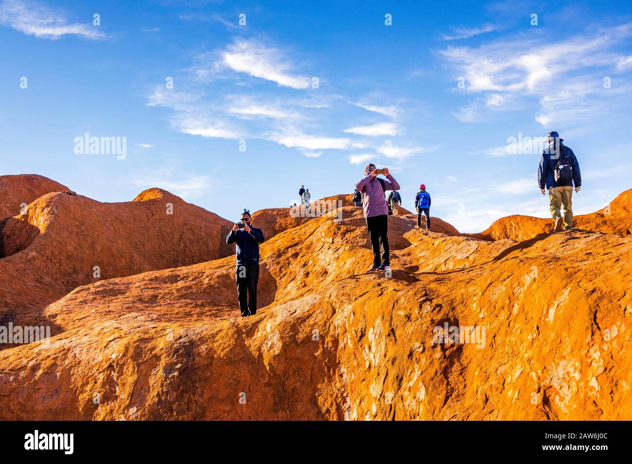 Tourists climb over the steep undulating terrain on top of Uluru ...