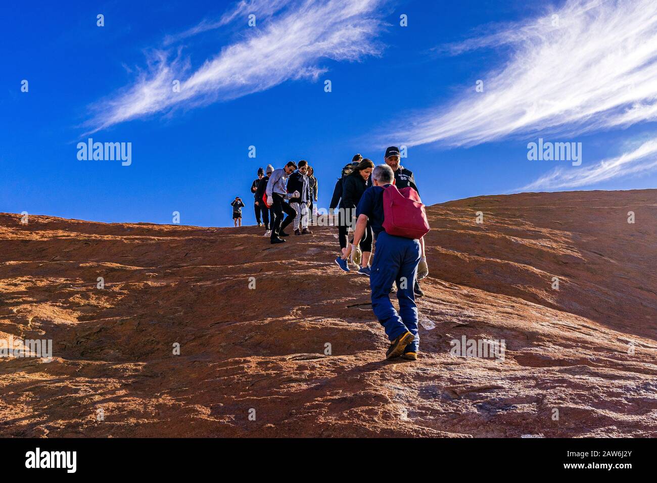 Tourists climb over the steep undulating terrain on top of Uluru ...