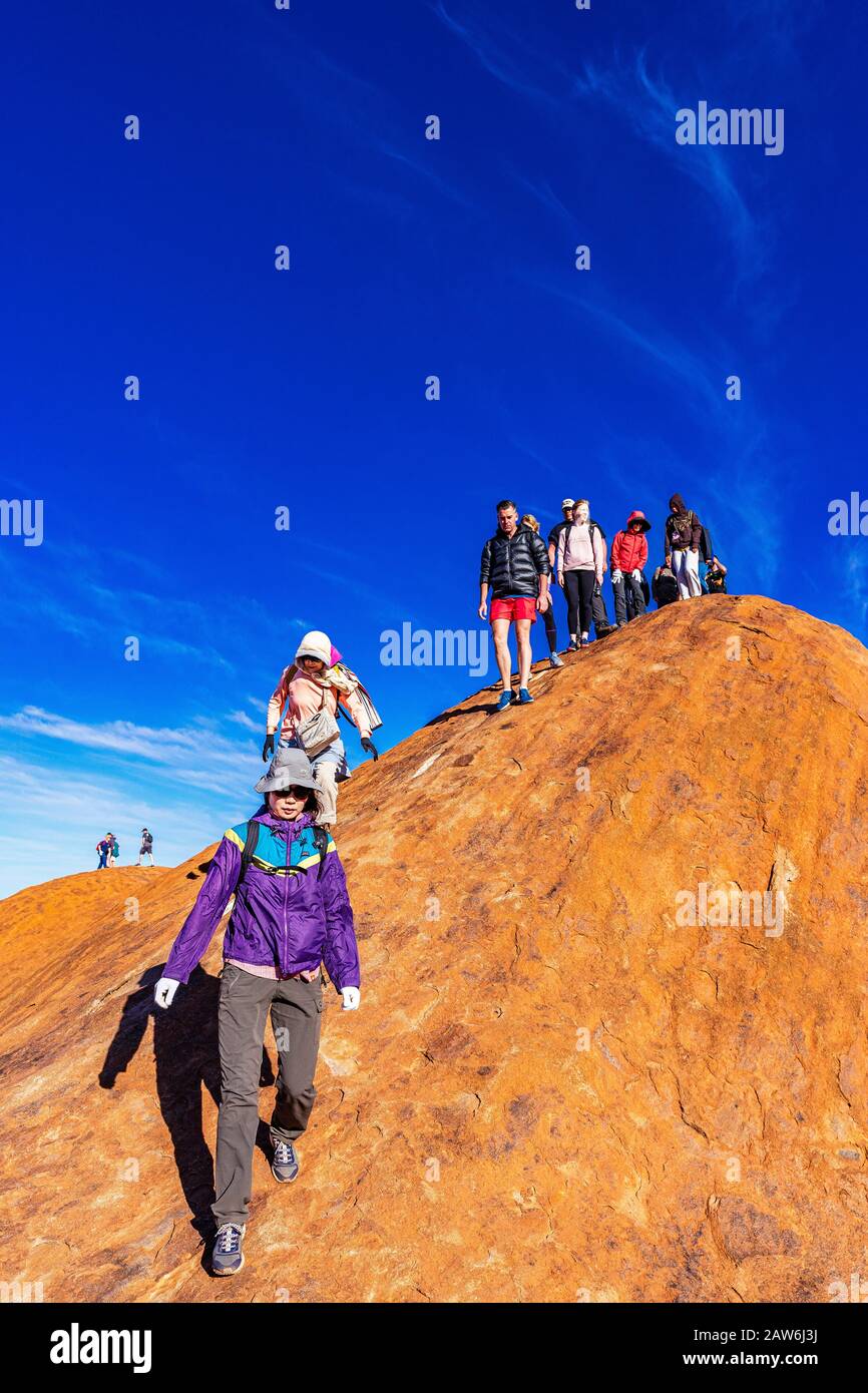 Tourists climb over the steep undulating terrain on top of Uluru ...