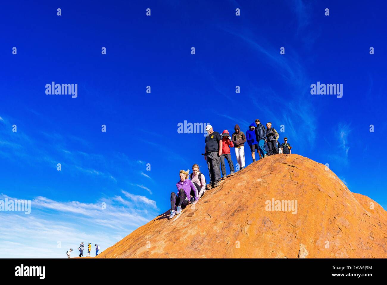 Tourists climb over the steep undulating terrain on top of Uluru ...