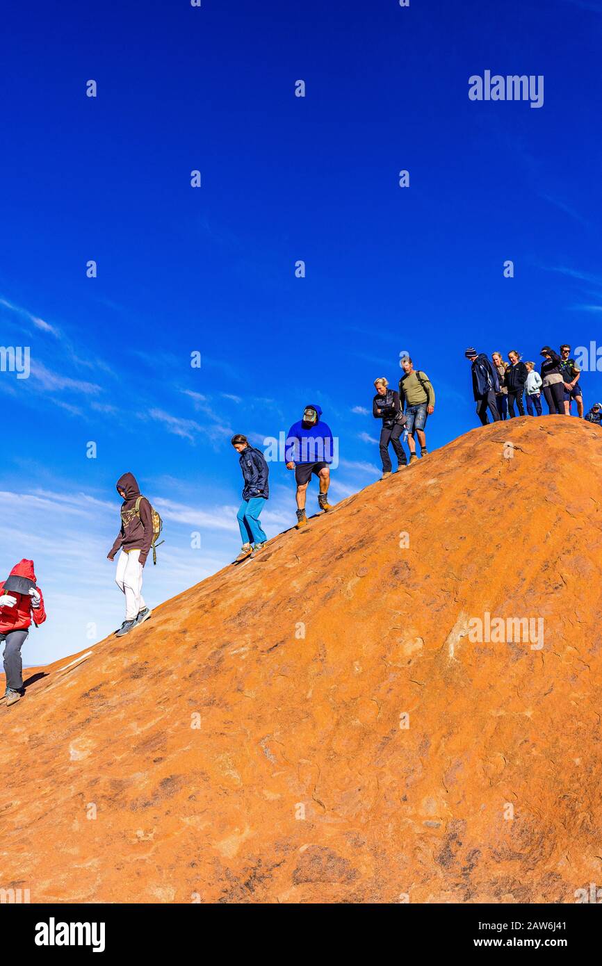 Tourists climb over the steep undulating terrain on top of Uluru ...