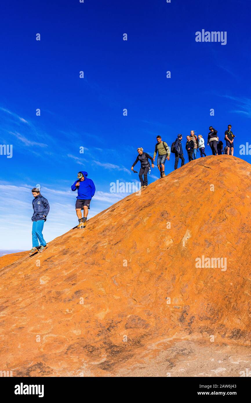 Tourists climb over the steep undulating terrain on top of Uluru ...