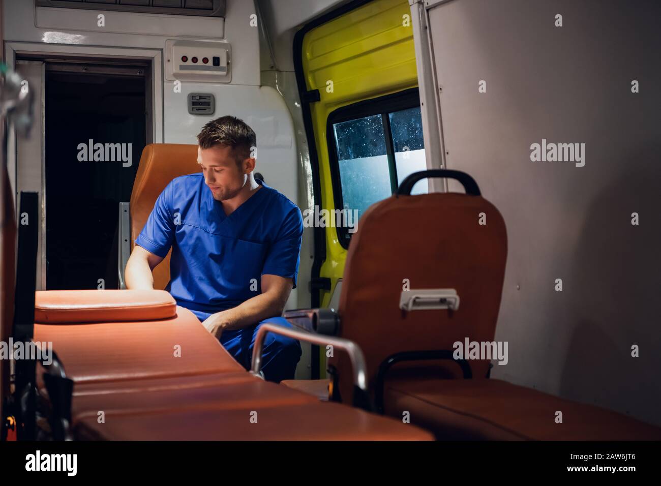 Paramedic In Blue Medical Uniform Sits In The Ambulance Car And Look