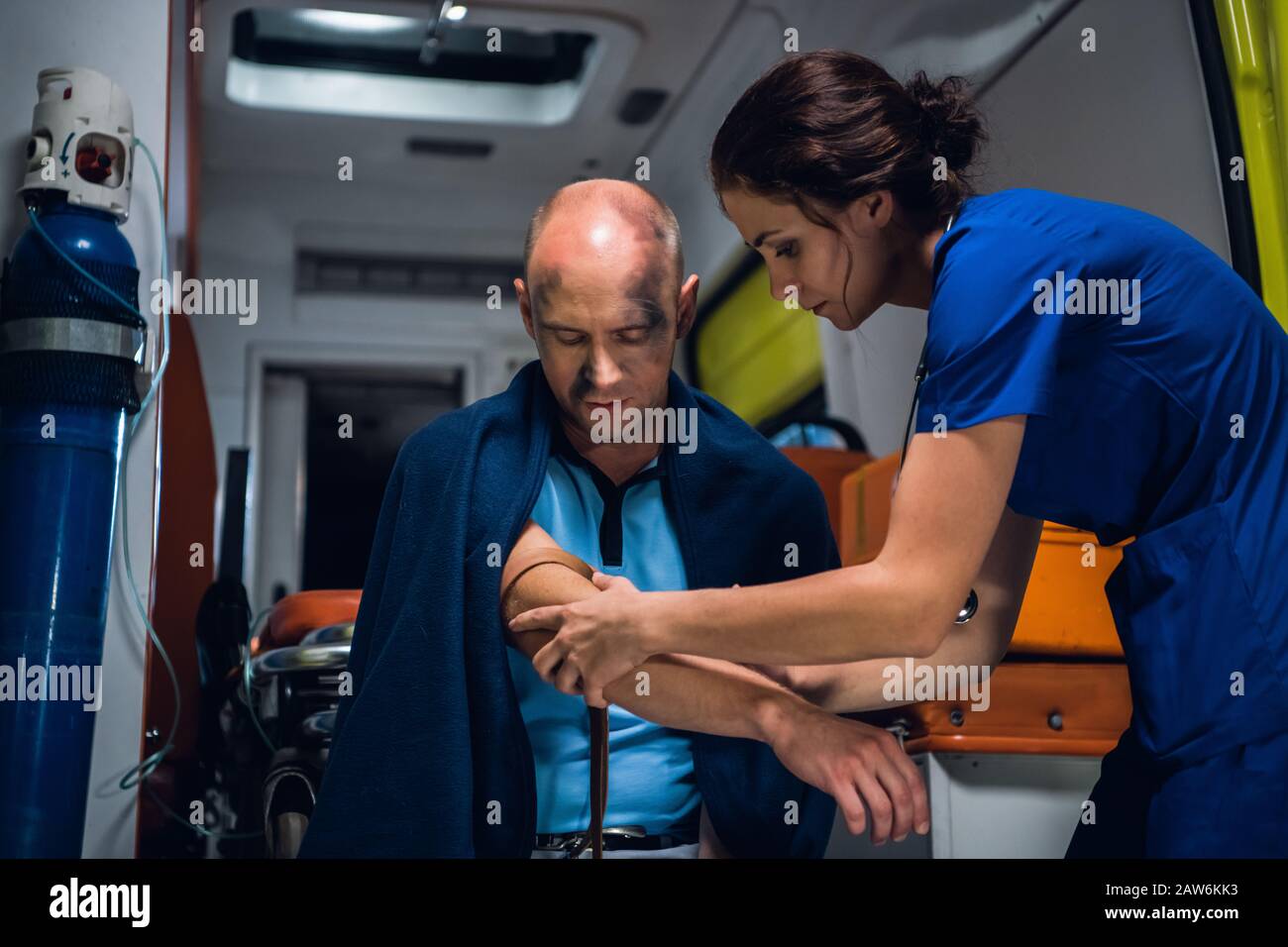 Woman in blue medical uniform wraps a tourniquet around a hand of ...