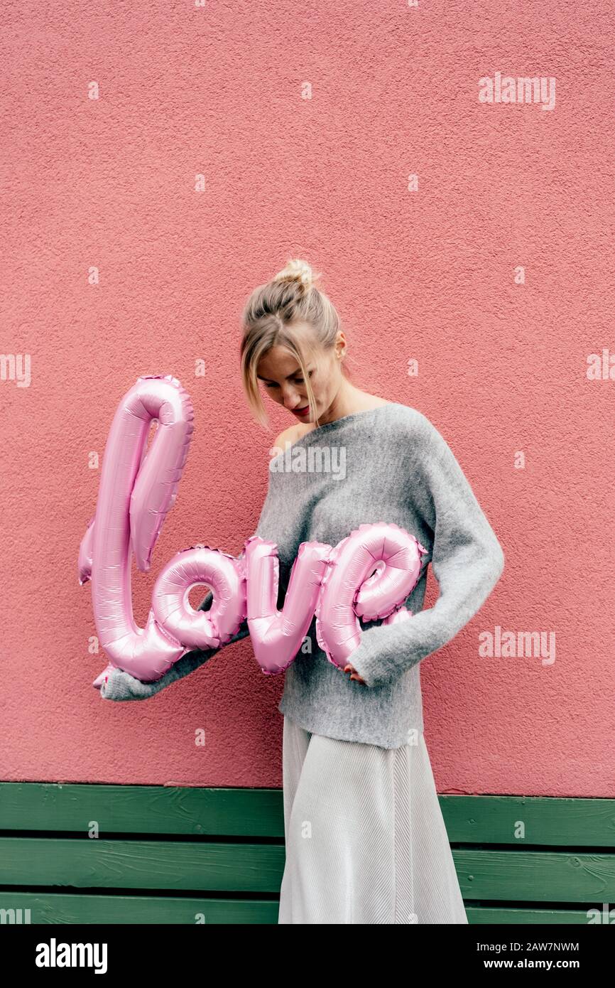 Cute blonde holds a big inflatable word LOVE standing against a pink ...