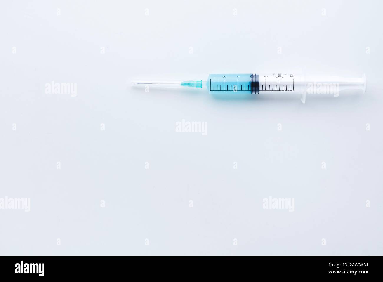 Single syringe filled with light blue liquid placed horizontally on ...