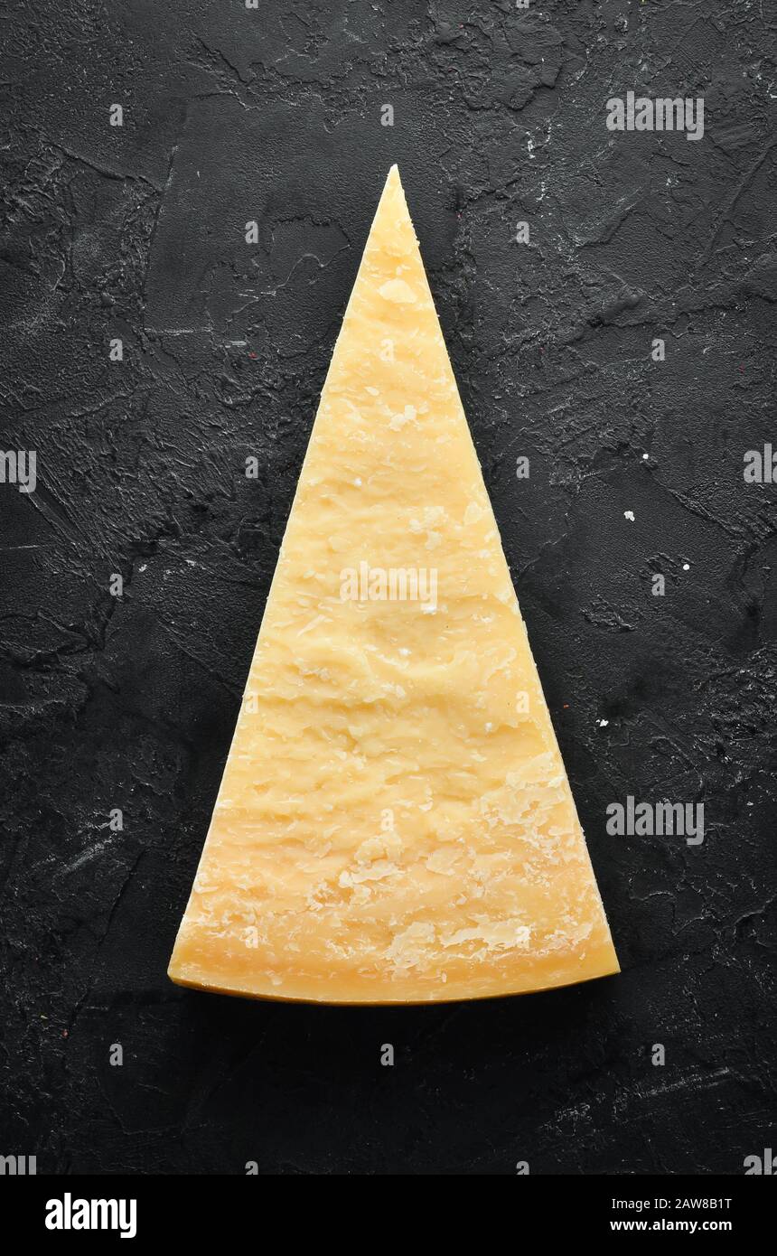 Piece of solid cheese on a black stone background. Parmesan. Top view ...