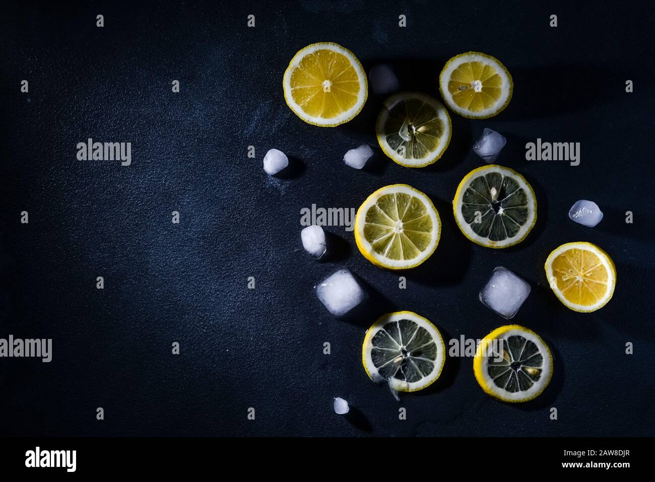 cut lemons with lemon slices and ice cubes against dark background. Top ...