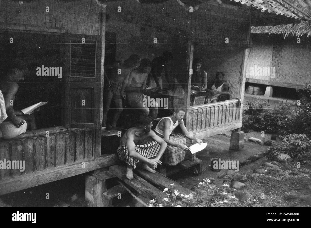 Bantam Dutch soldiers, some wearing sarongs, relax on a porch of a ...