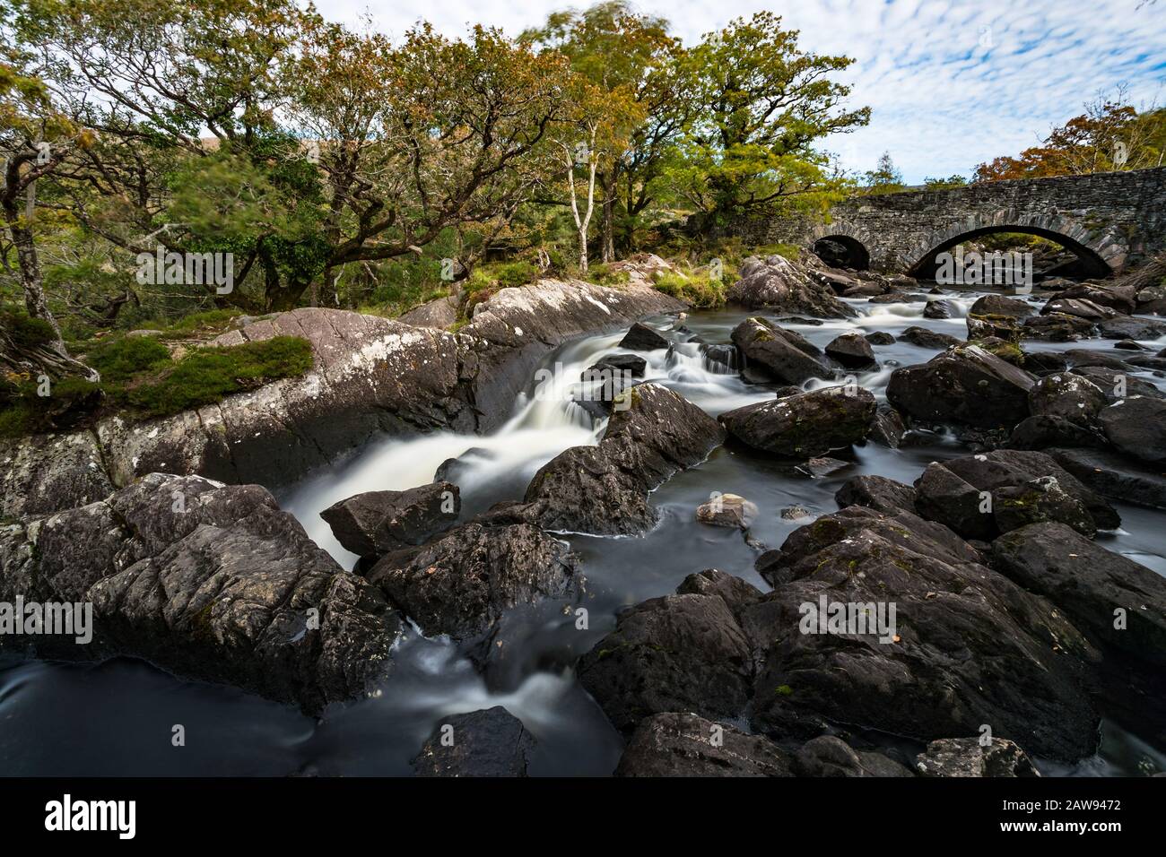 An old stone bridge across a winding River stram in the rocky terrain ...