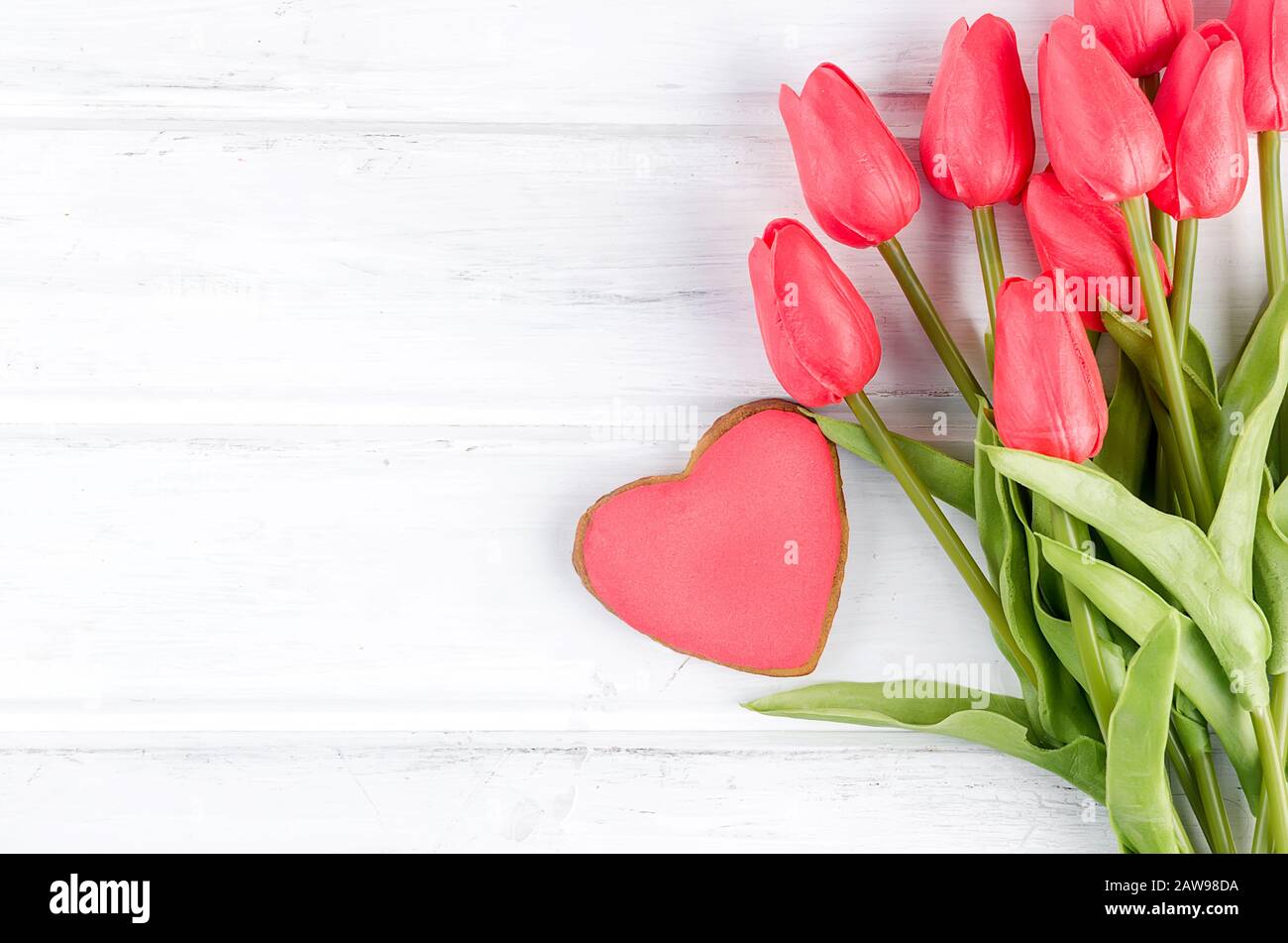red gingerbread heart and a bouquet of tulips lying on white wooden ...