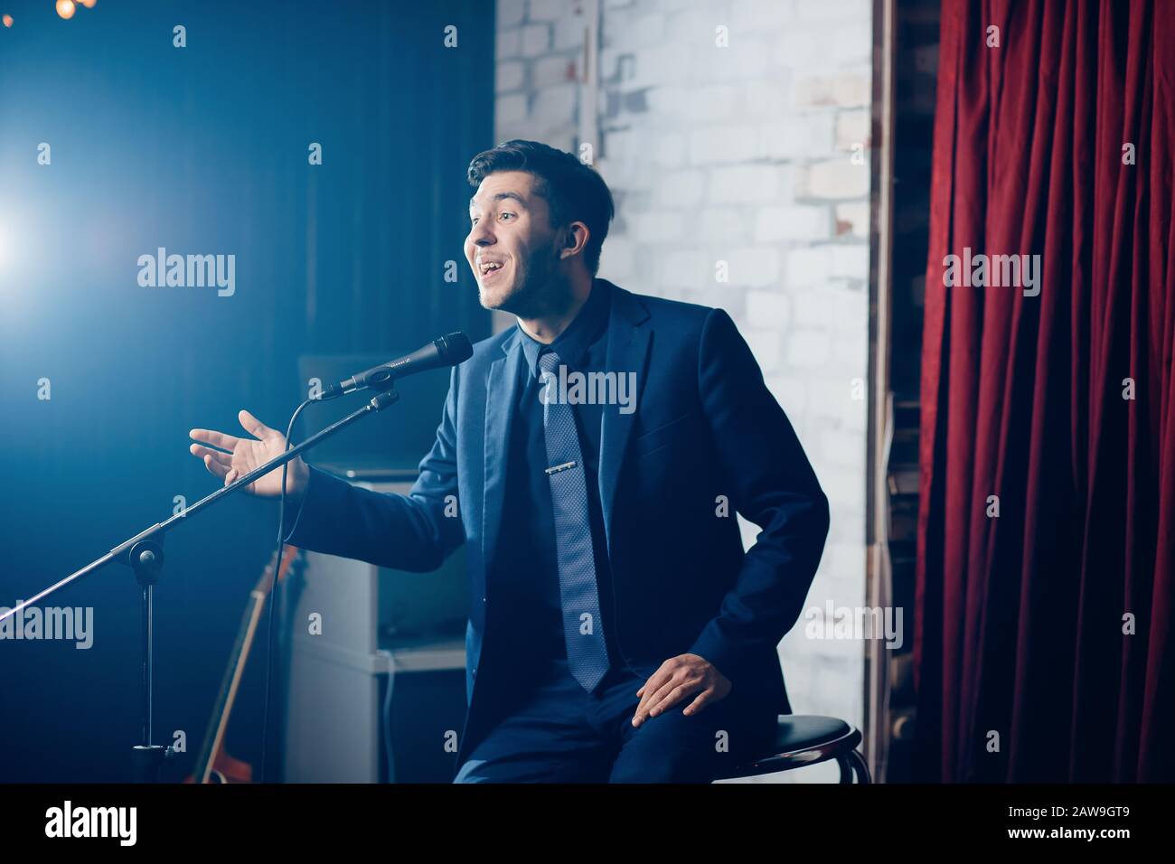 Stand up comedian on stage. Young man talks joke into microphone or ...