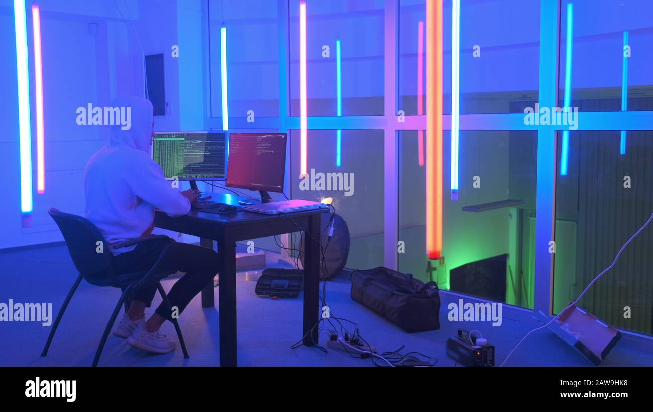 Hacker working place: hacker working in a room with colored neon lights ...