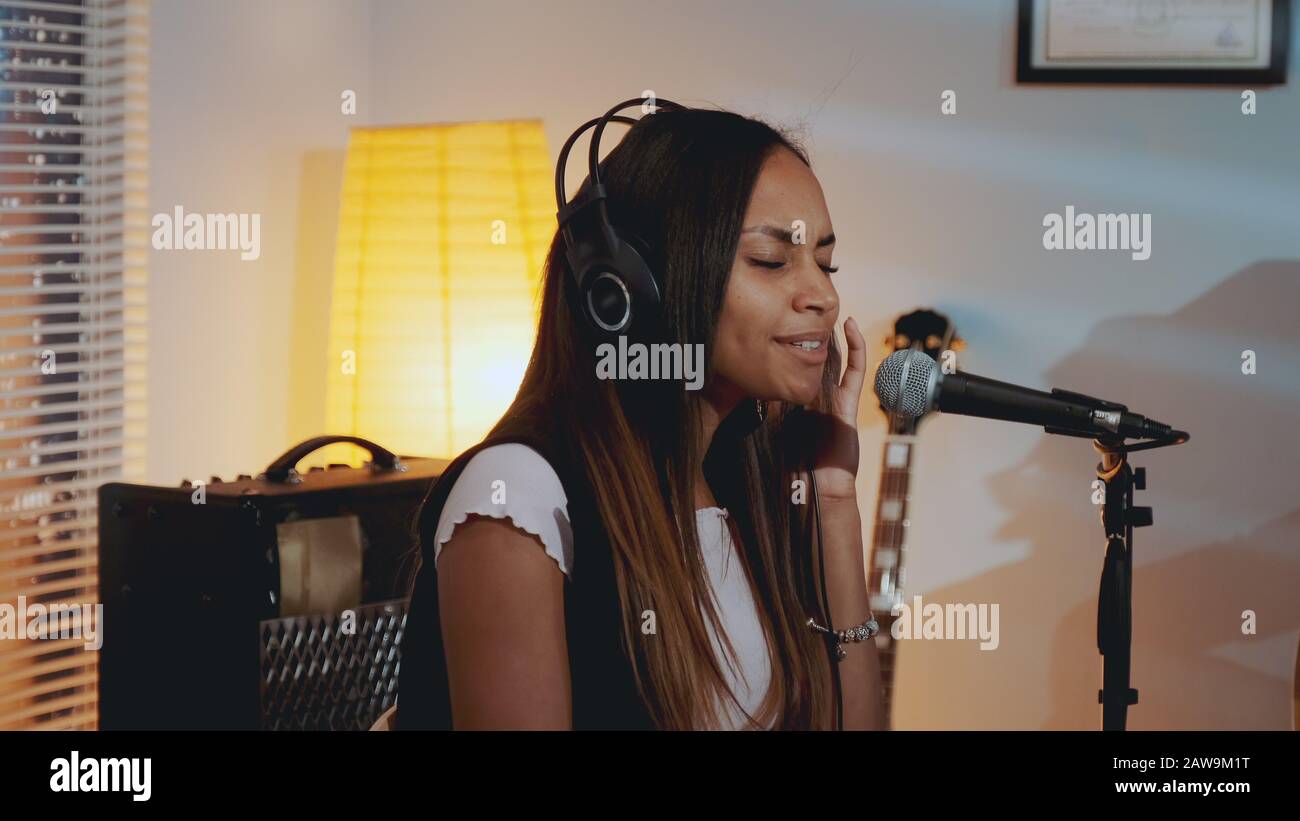 Black female vocalist in headphone recording her new song in home ...