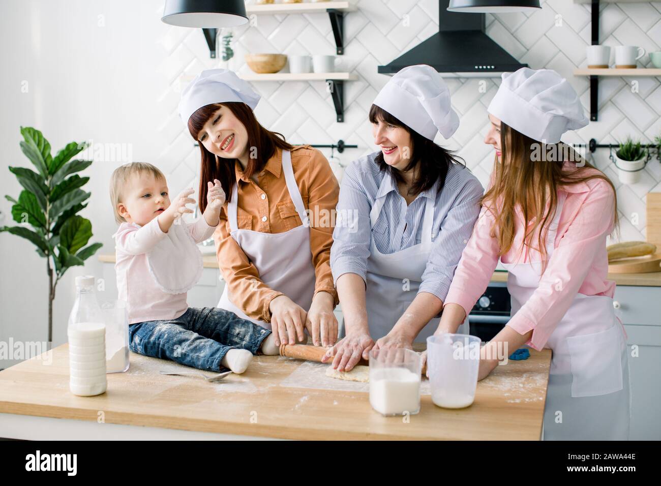 Smiling middle aged woman in kitchen apron rolling out dough and two ...