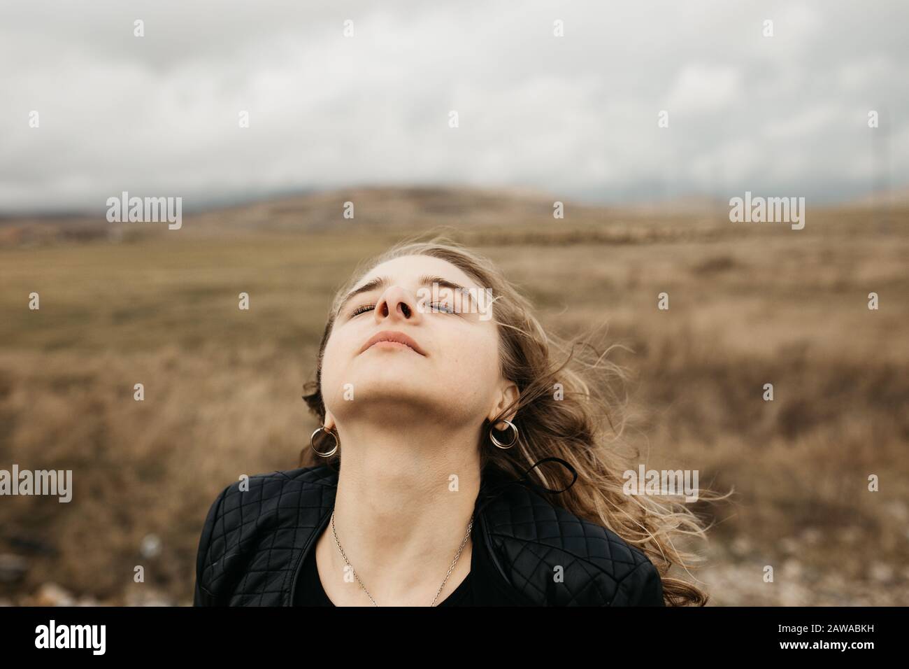 Portrait of young woman with hair blowing in the wind. She is wearing a ...