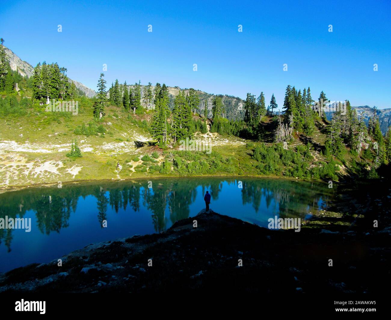 Male hiker standing by alpine lake in North Cascades National Park ...