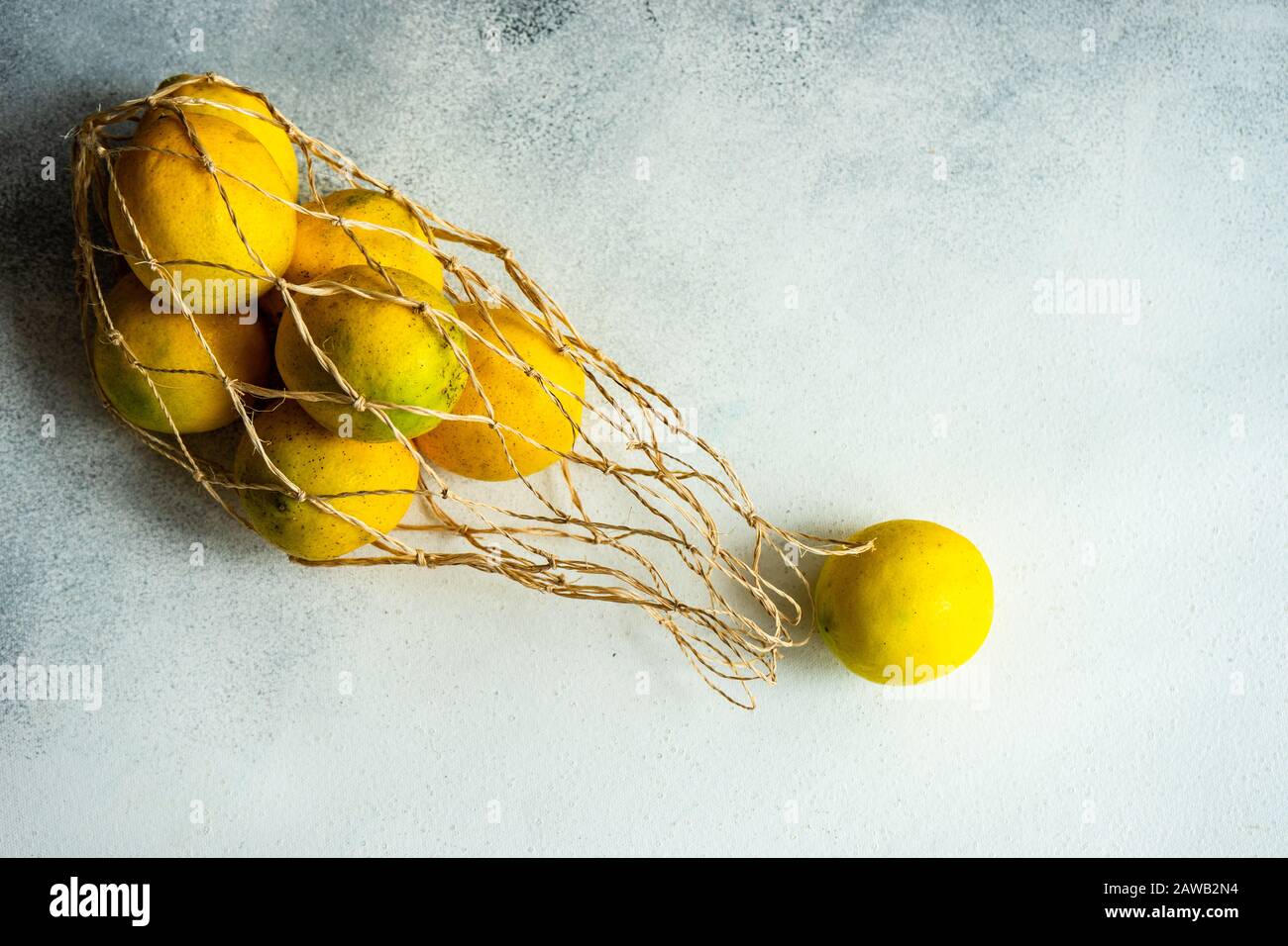 Organic yellow lemons in string bag on stone background with copy space ...