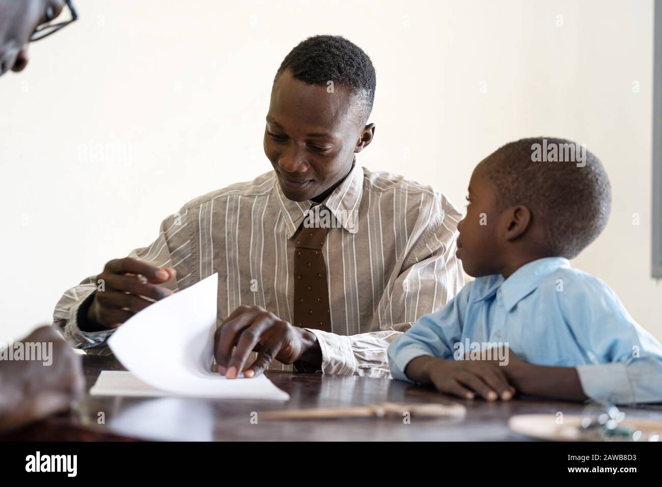 African dad and son signing papers documents to enroll child in school ...