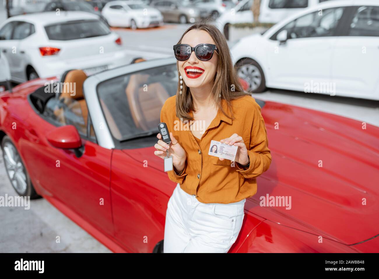 Portrait of a beautiful young woman standing with driver's license and ...