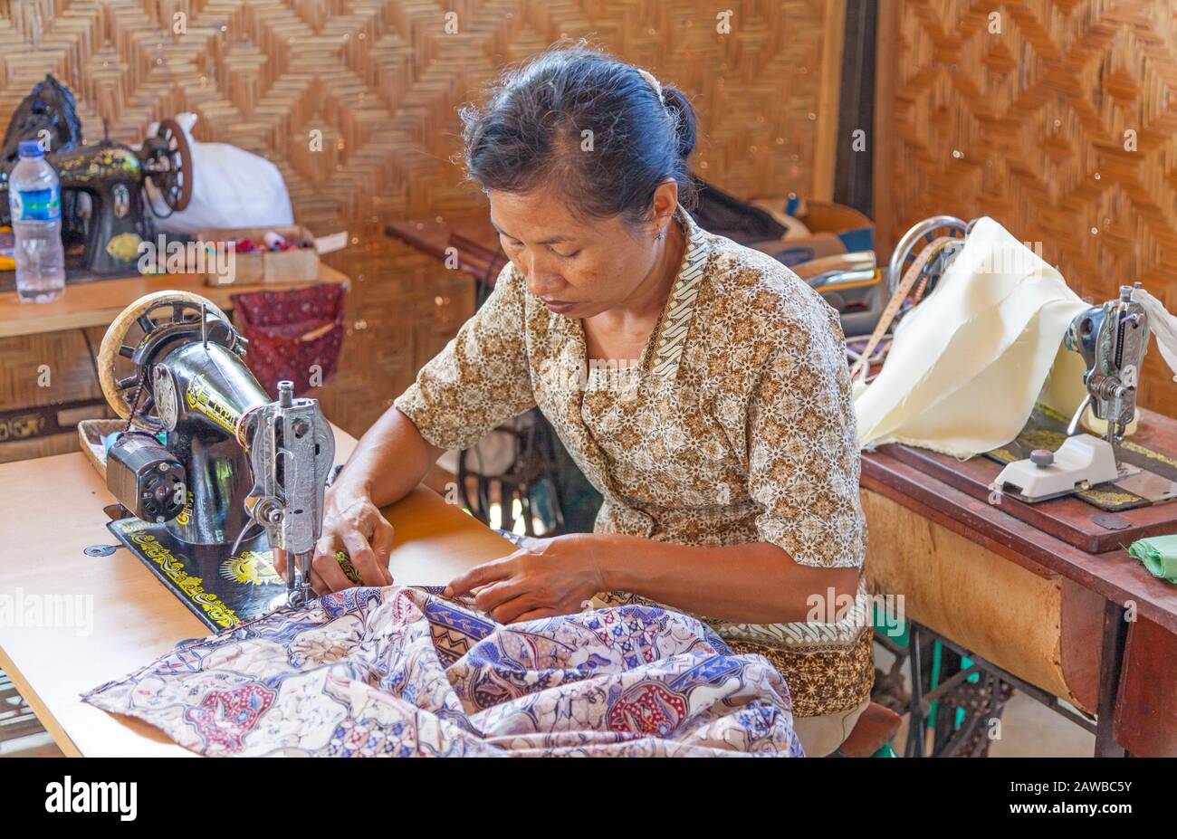 An unidentified Balinese woman sewing a traditional batik garment at ...