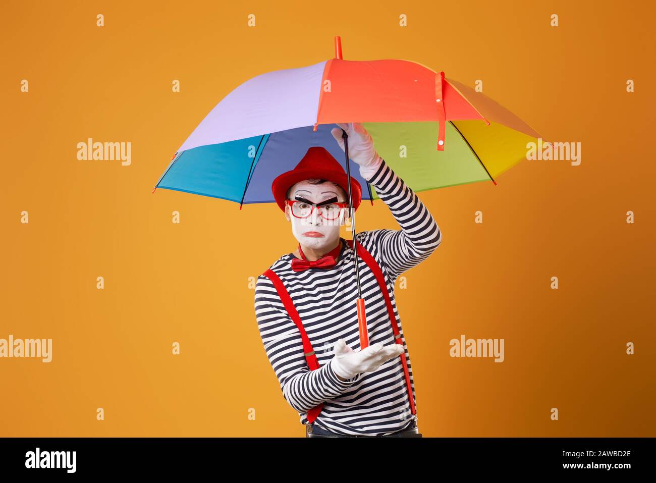 Serious mime with multi-colored umbrella on empty orange background in ...