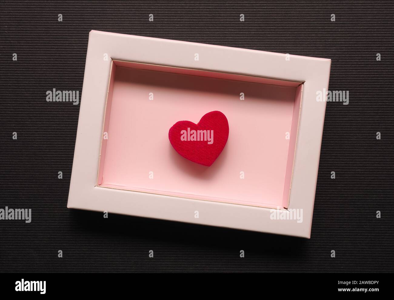 Red wooden heart shape in a paper gift box on a modern dark background ...