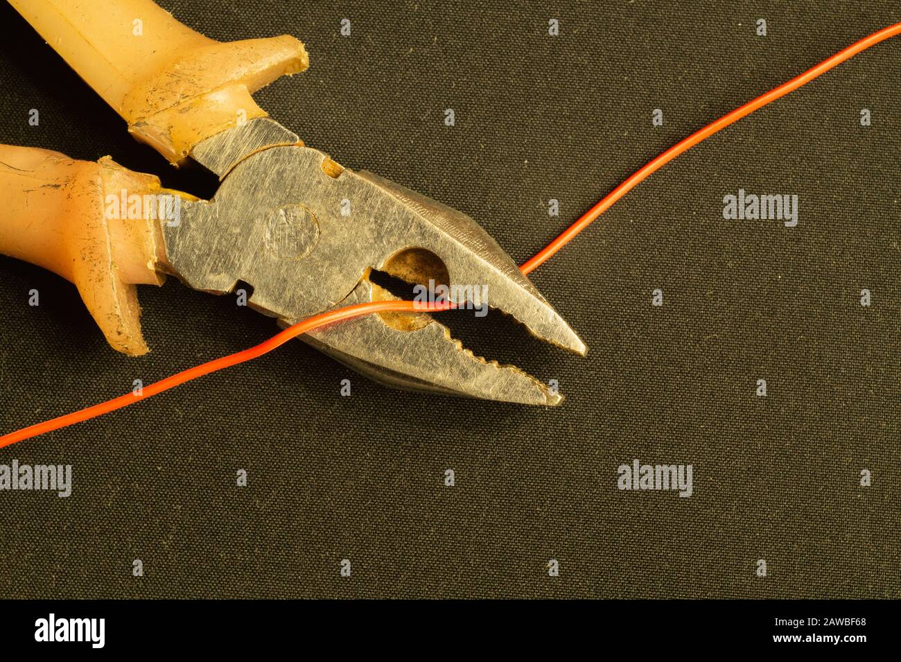 Pliers cuts a red wire on black background. pliers with orange handles ...