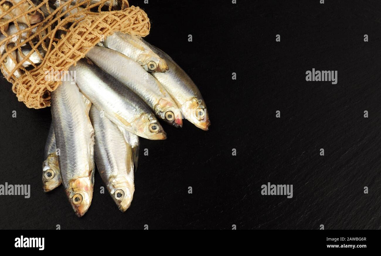 Group of fresh fish sprats in a string netting bag on a slate stone ...