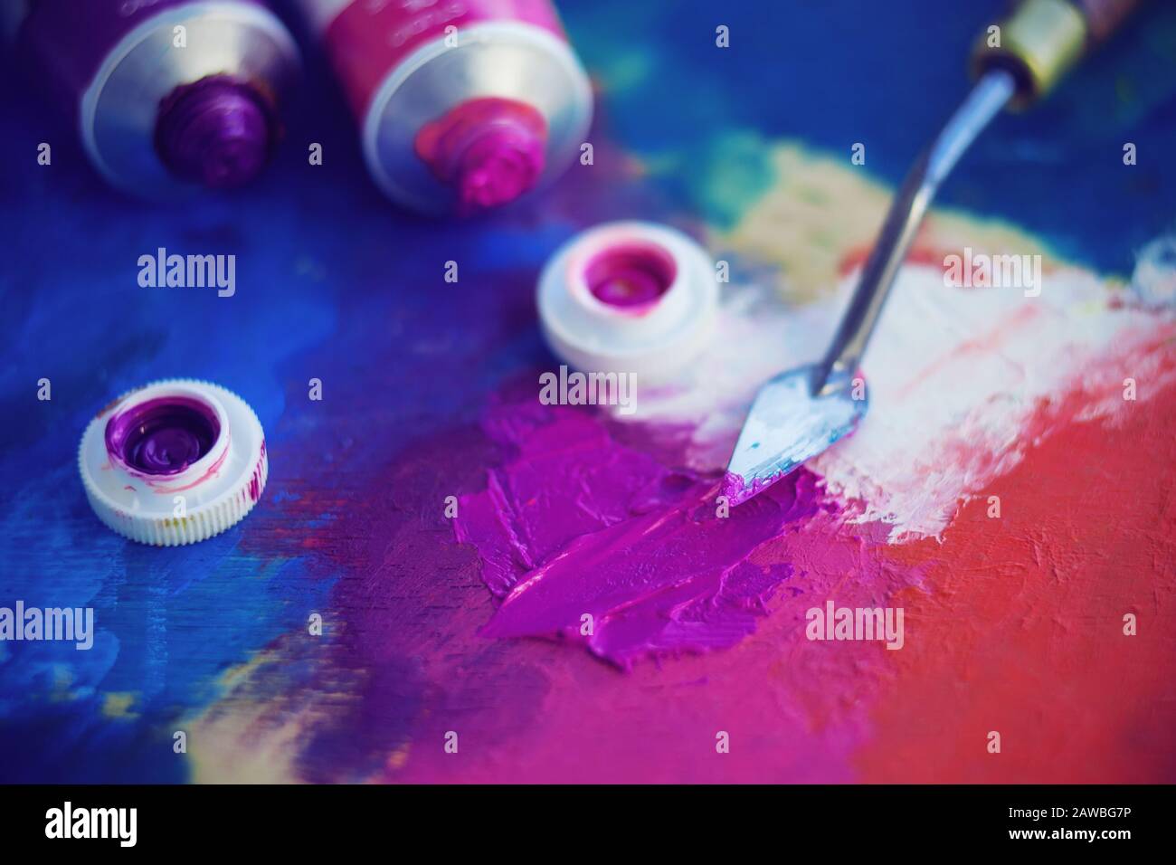 Open tubes of purple and pink colors paint and a palette knife are on ...